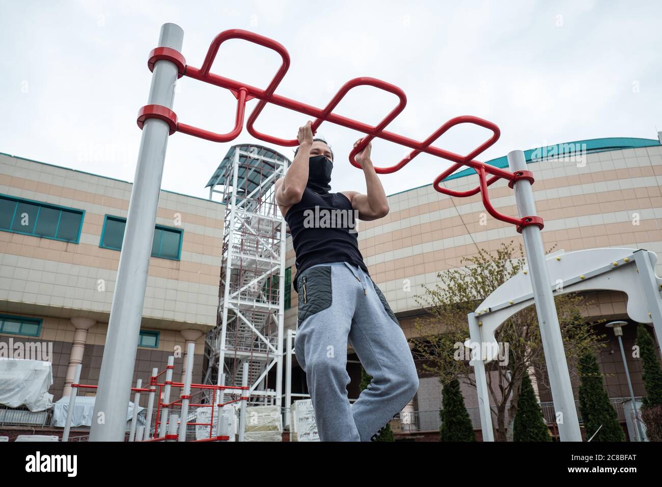 The guy is pushing up on the bars, in a black T-shirt and mask, in ...