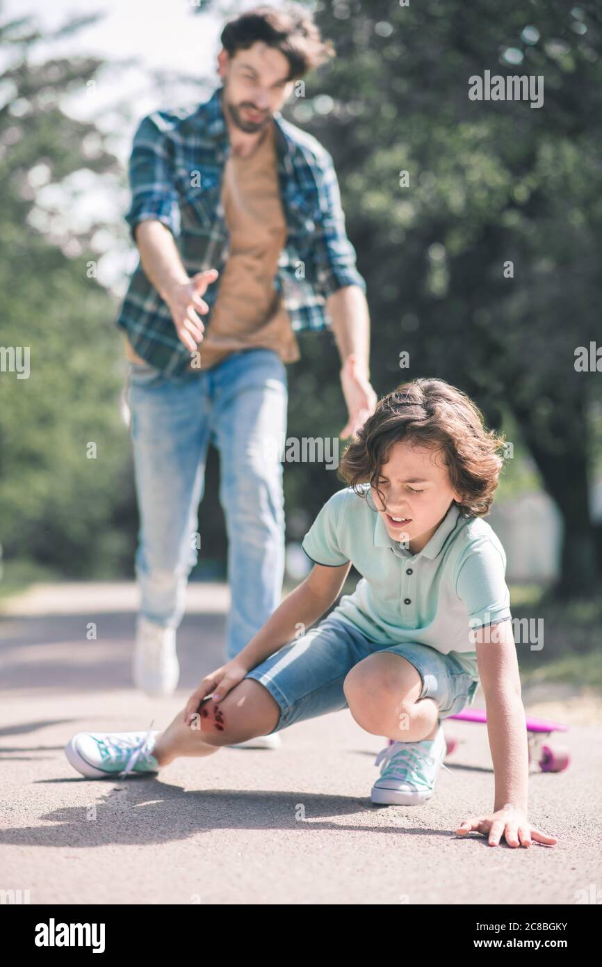 Dark-haired boy falling down on the ground, his father rushing to help ...