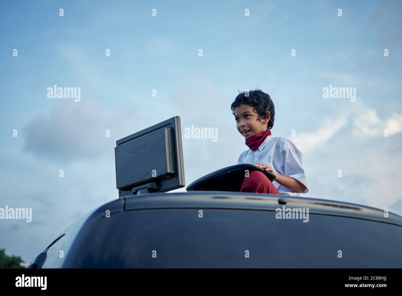 Boy in school uniform playing internet games on top of car roof, New ...