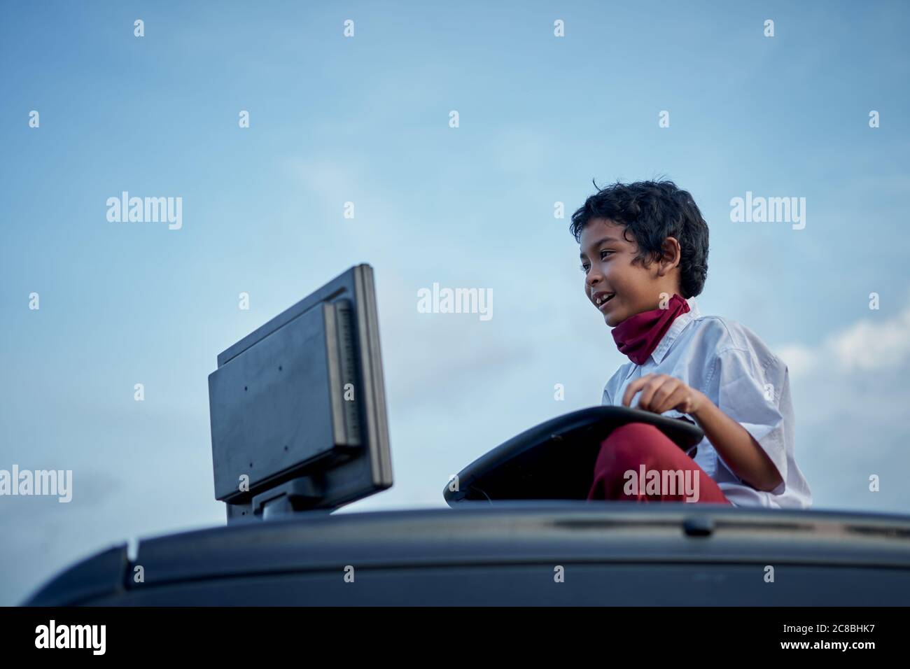 Boy in school uniform playing internet games on top of car roof, New ...