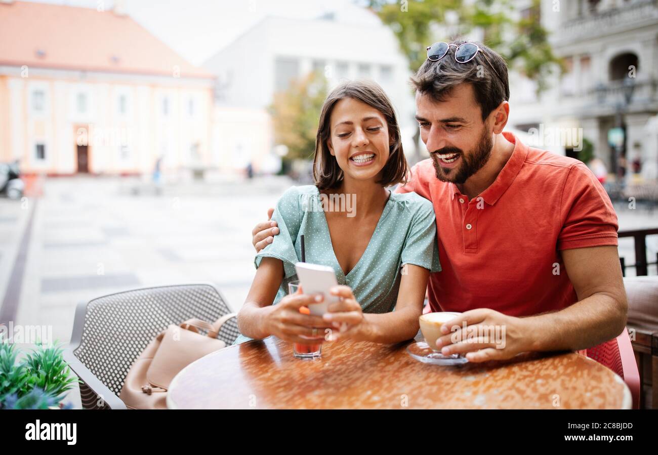 Embracing couple using mobile phone, smiling and talking in cafe Stock ...