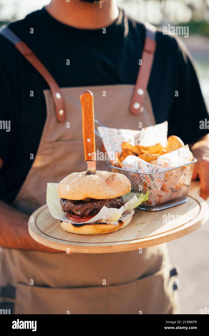 Waiter serving a delicious burger, fries and sauce served on wooden ...
