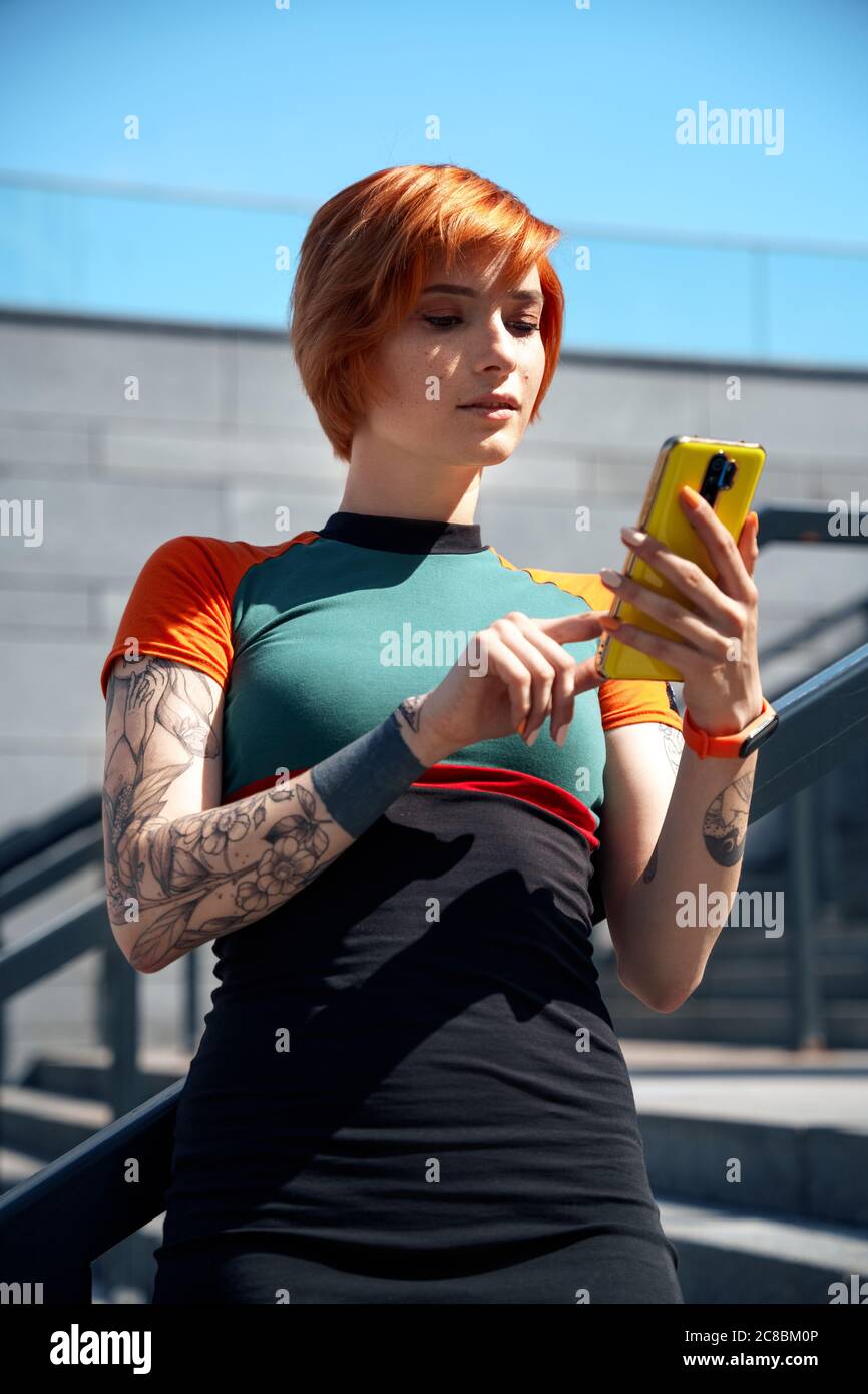 A Ginger Hipster Girl In A Stylish Dress Is Using An App On A