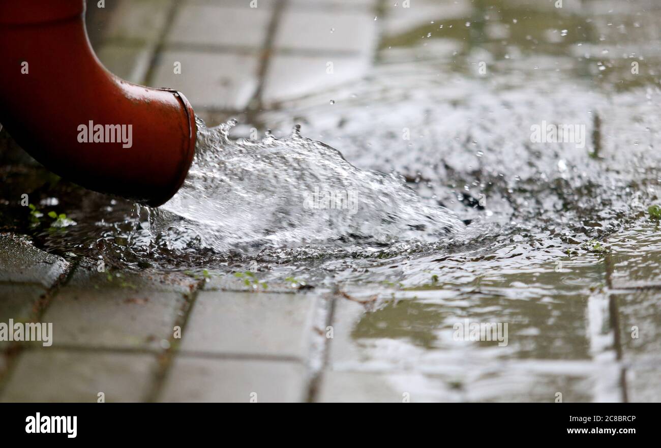 Rain water is pouring from the green draining gutter on the pavement ...