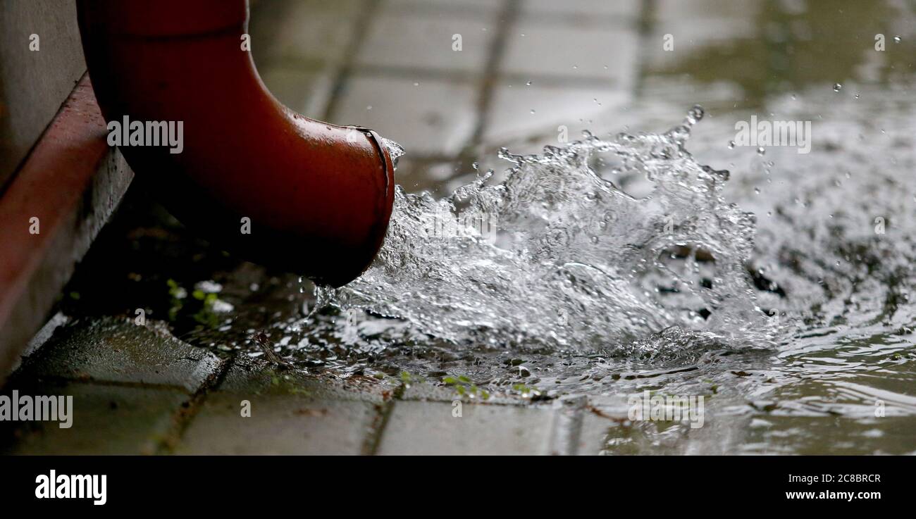 Rain water is pouring from the green draining gutter on the pavement ...