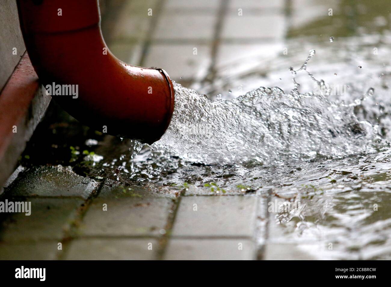 Rain water is pouring from the green draining gutter on the pavement ...
