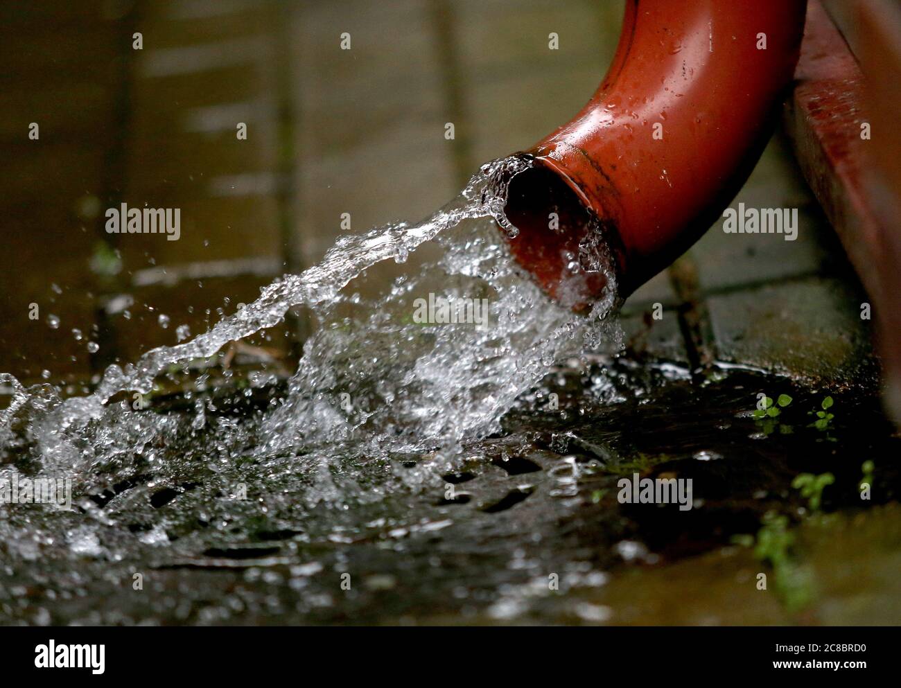 Rain water is pouring from the green draining gutter on the pavement ...
