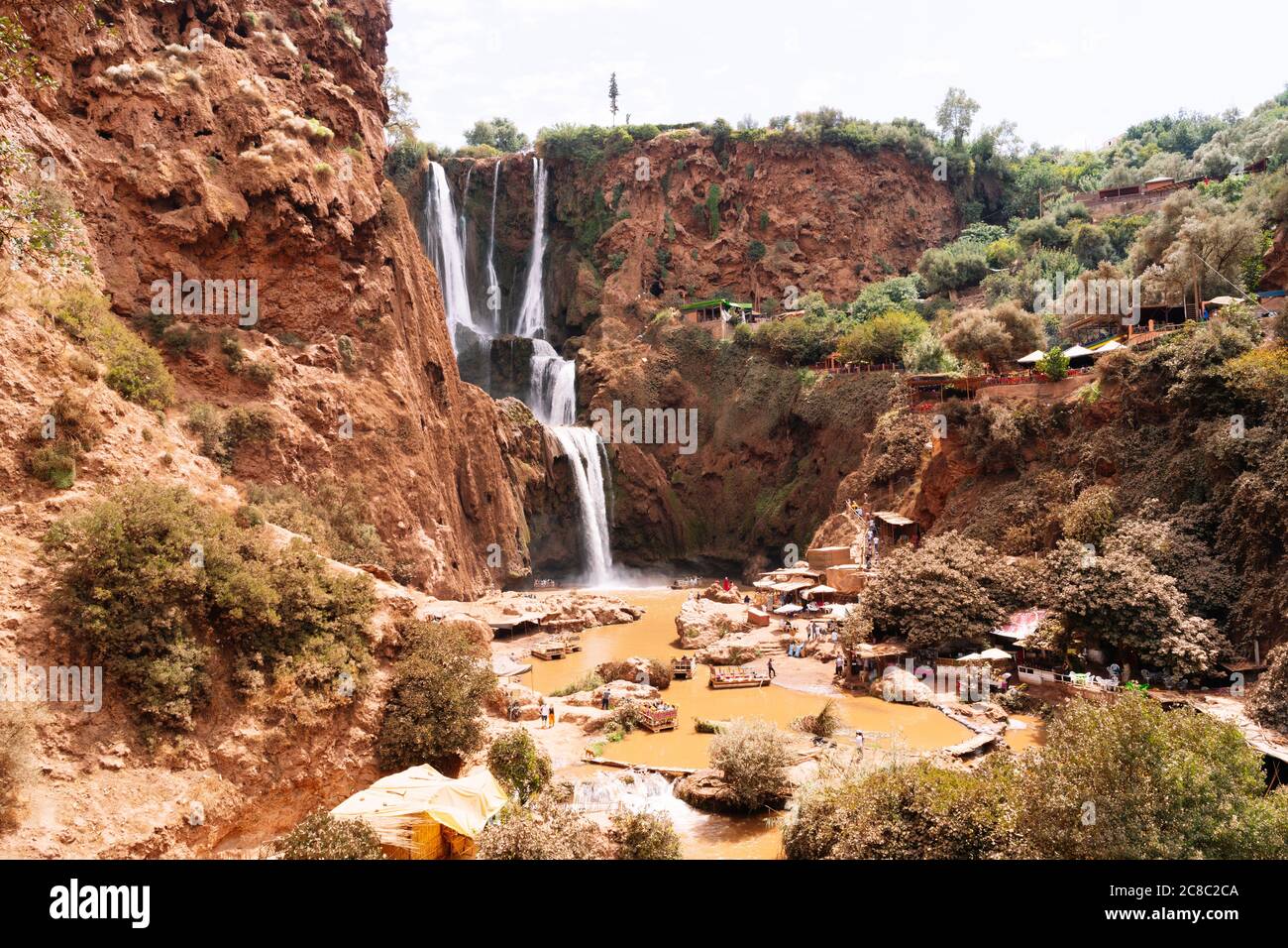 Waterfalls with a small lake in an arid terrain with several people ...