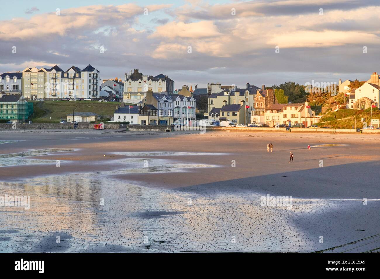 A near deserted Port Erin beach with deep shadow cast by the setting ...
