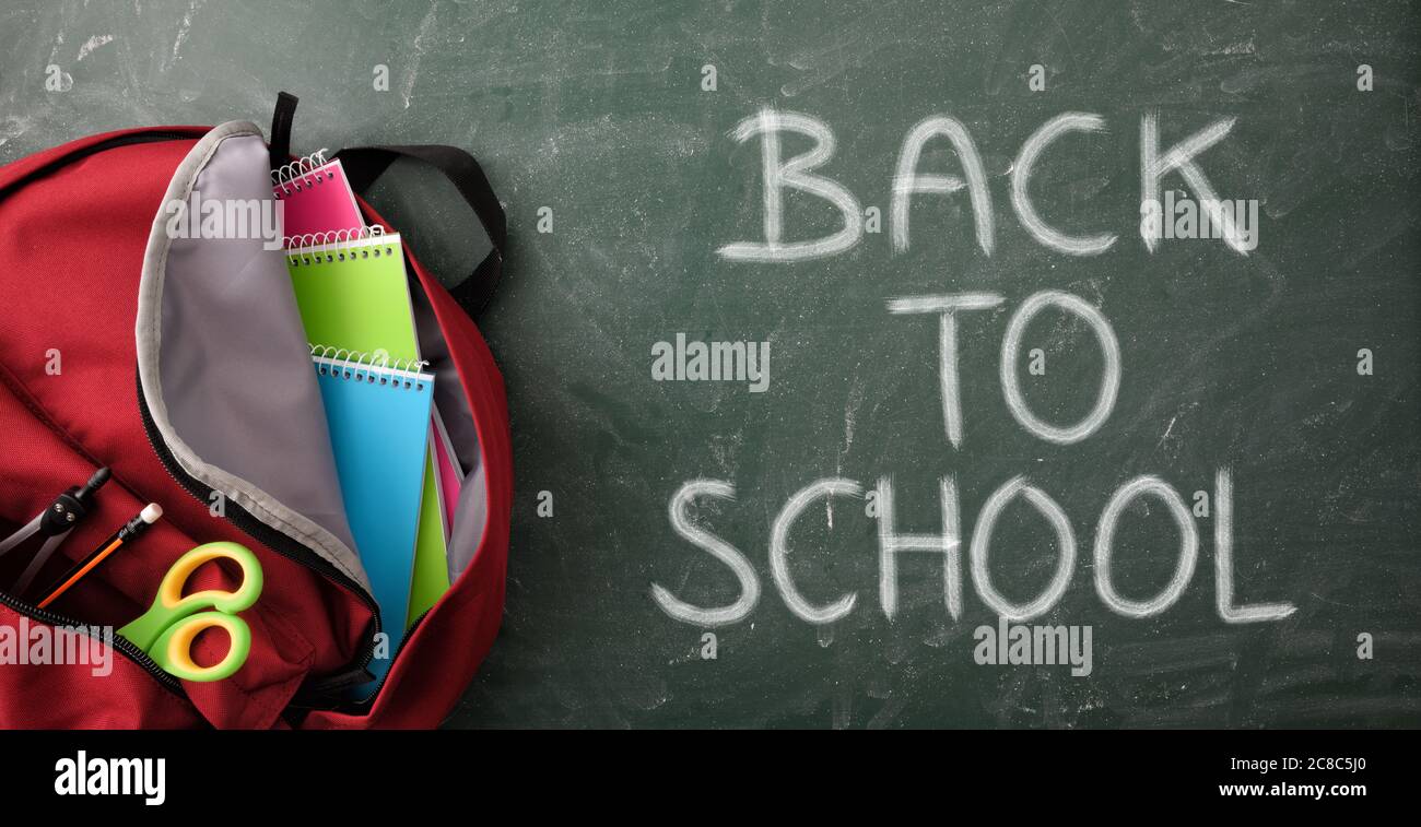 Detail of backpack full of school supplies on green blackboard with ...