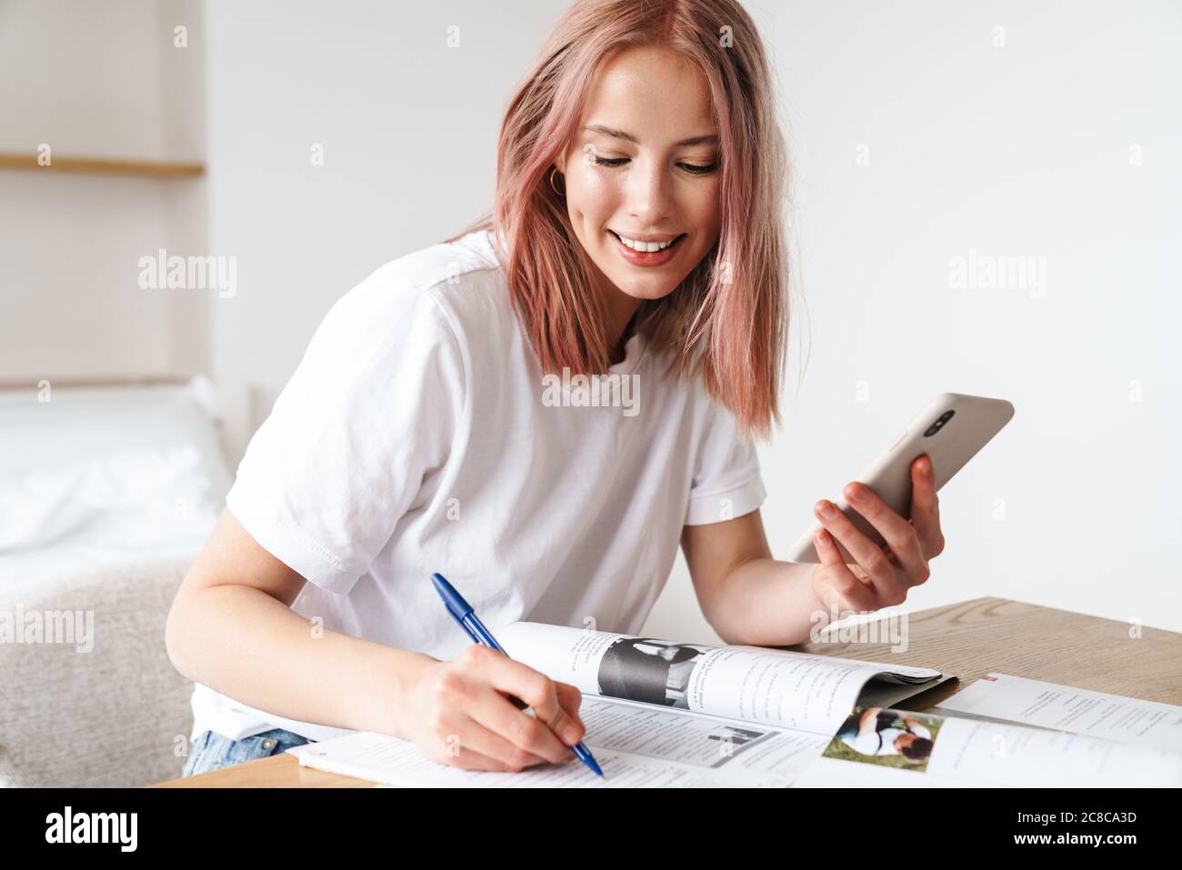 Image of smiling caucasian woman using smartphone while doing homework ...