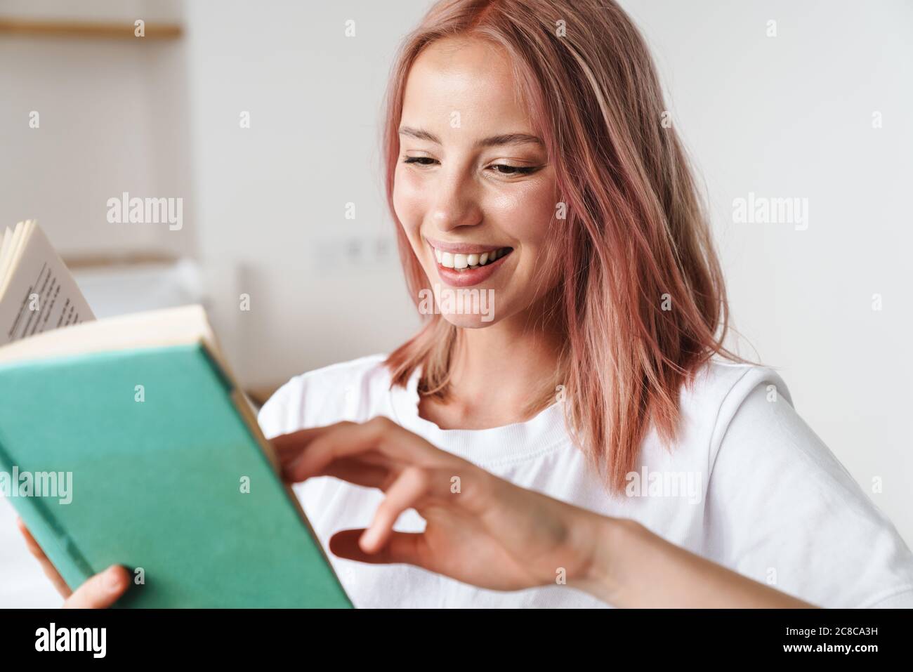 Image of joyful pretty woman with pink hair reading book and smiling ...