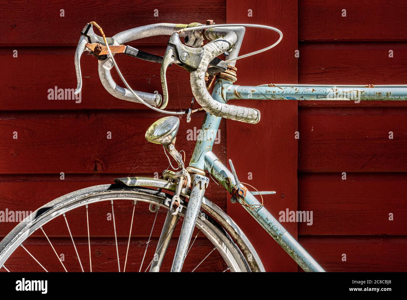 An old, blue and rusty racing bike leaning against a red, wooden wall ...