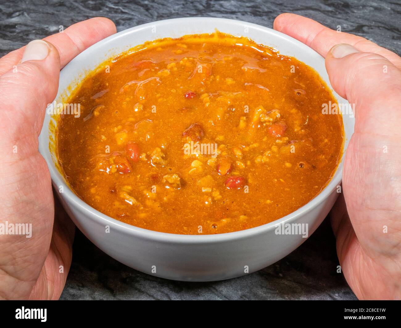 Closeup of a man’s hands around a bowl of hot chilli con carne on a ...