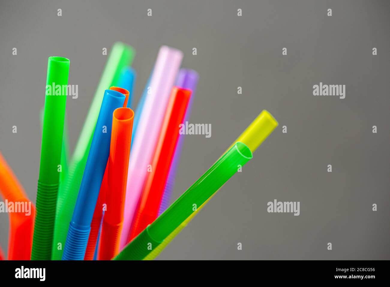Multi colored plastic straws in a jar in front of a grey background ...