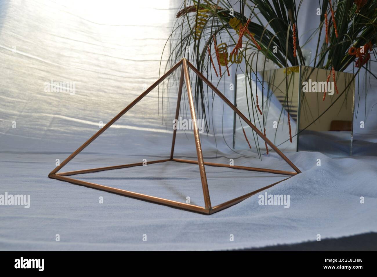 Copper pyramid with lighting, with glass vase and flowers in side view ...