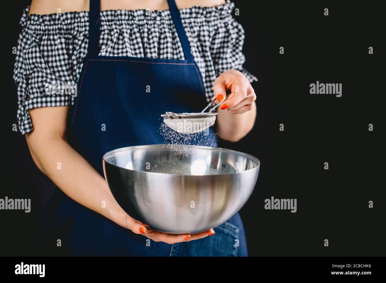Woman sifting flour through sieve into steel dish, preparing for baking ...