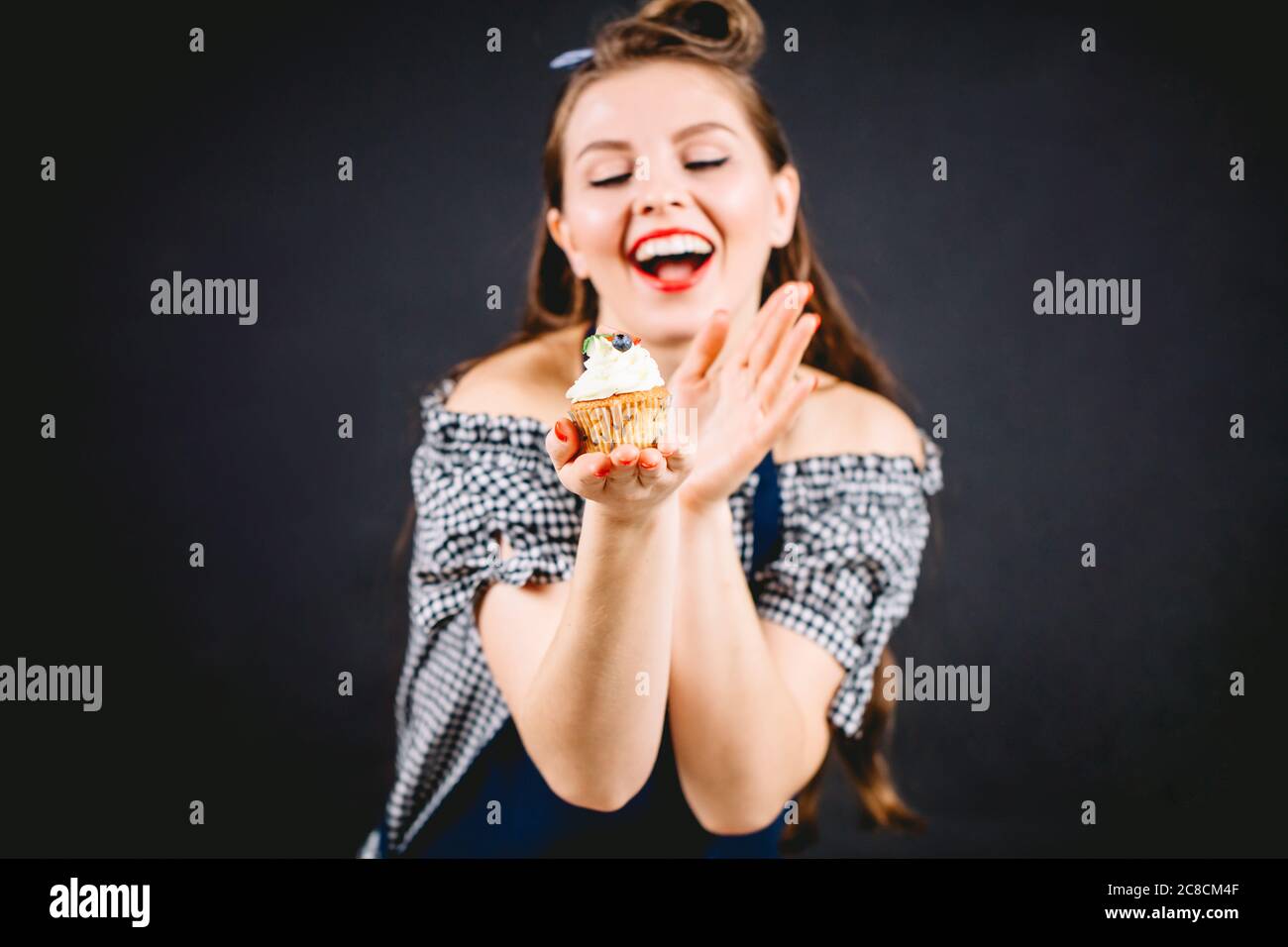 Young woman with delight expression invitng us to taste cupcake in her ...