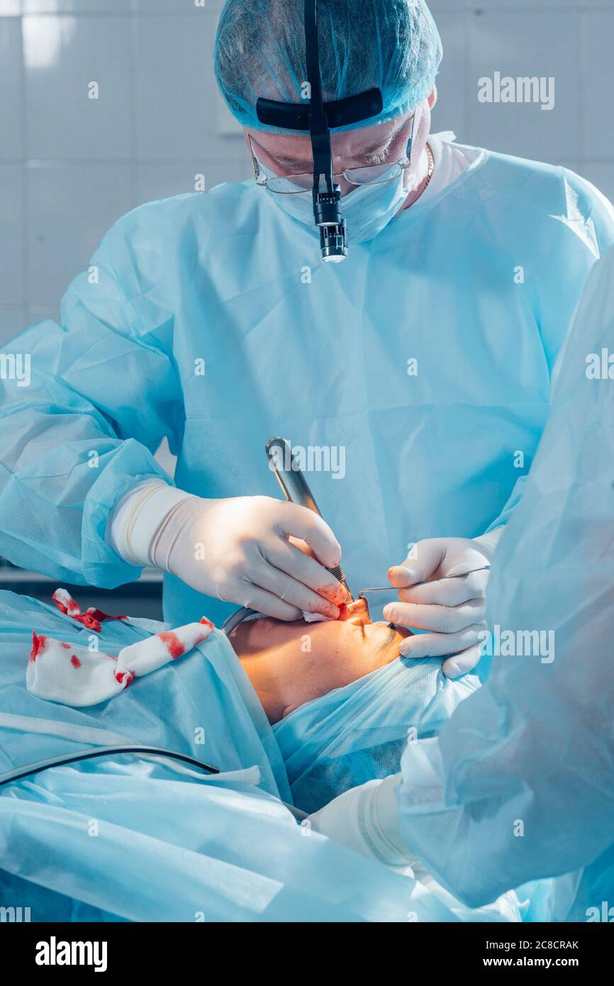 Surgeon performing cosmetic surgery on nose in hospital operating room ...