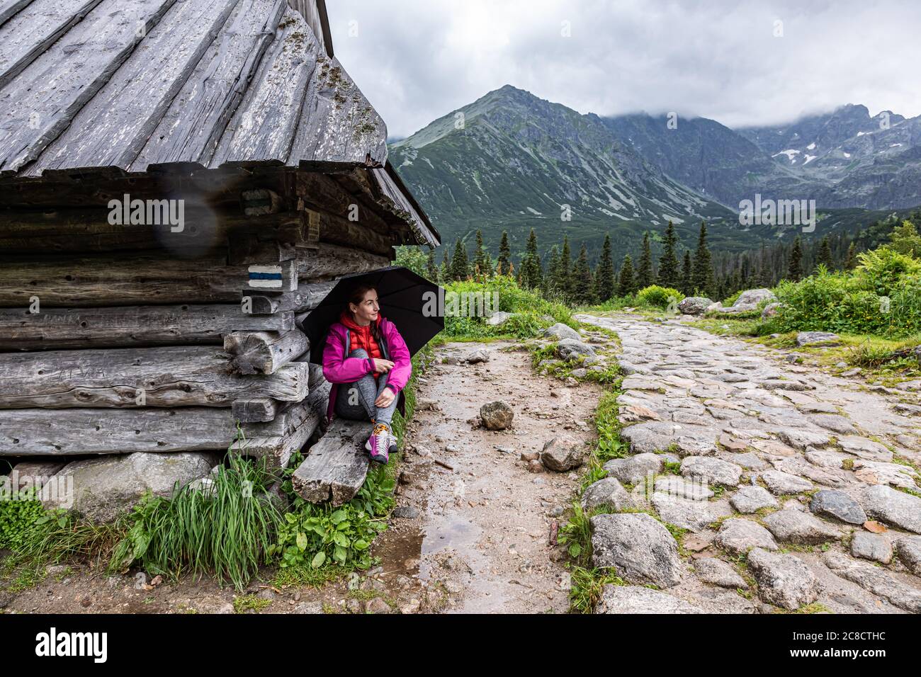 woman hiding from rain under a roof of mountain shelter in Tatra ...