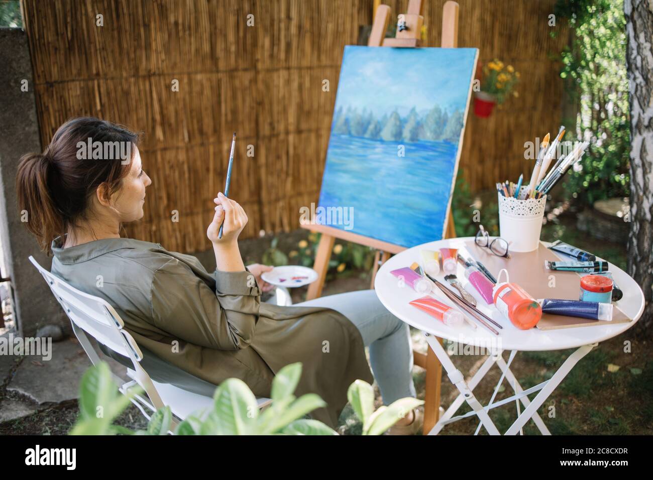 Side view of female painter sitting in front of painting Stock Photo ...