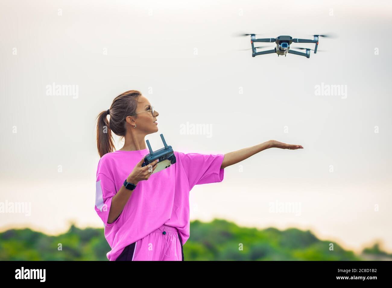 Stylish lady in pink clothes holding remote control and landing drone ...