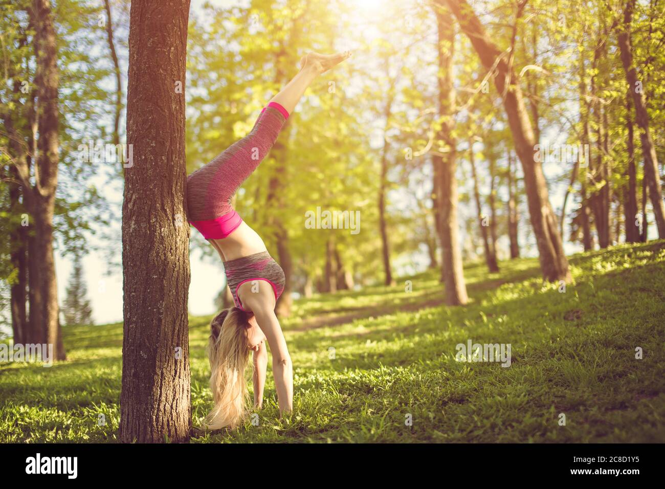young woman practicing inversion balancing yoga pose handstand in park ...