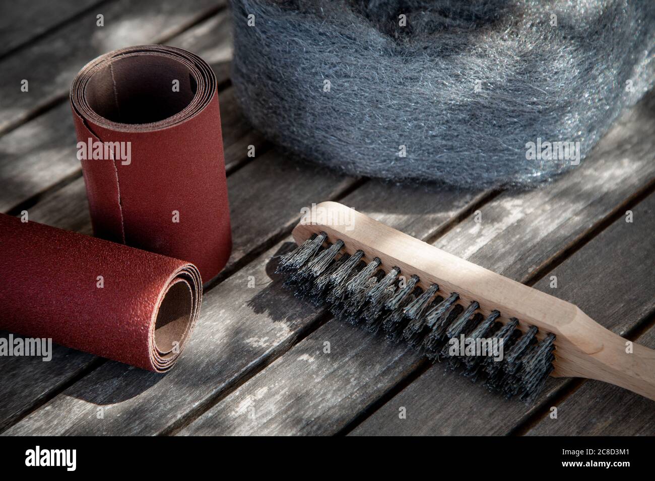 Wire brush and sandpaper lying on badly maintained wooden garden table ...
