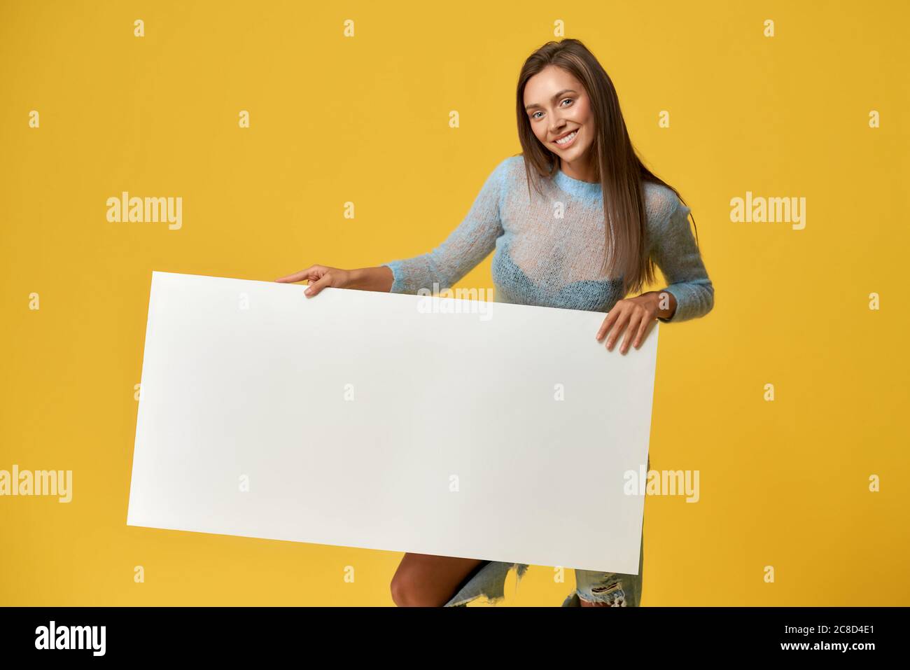 Front view of cheerful young woman holding white mock up placard for ...