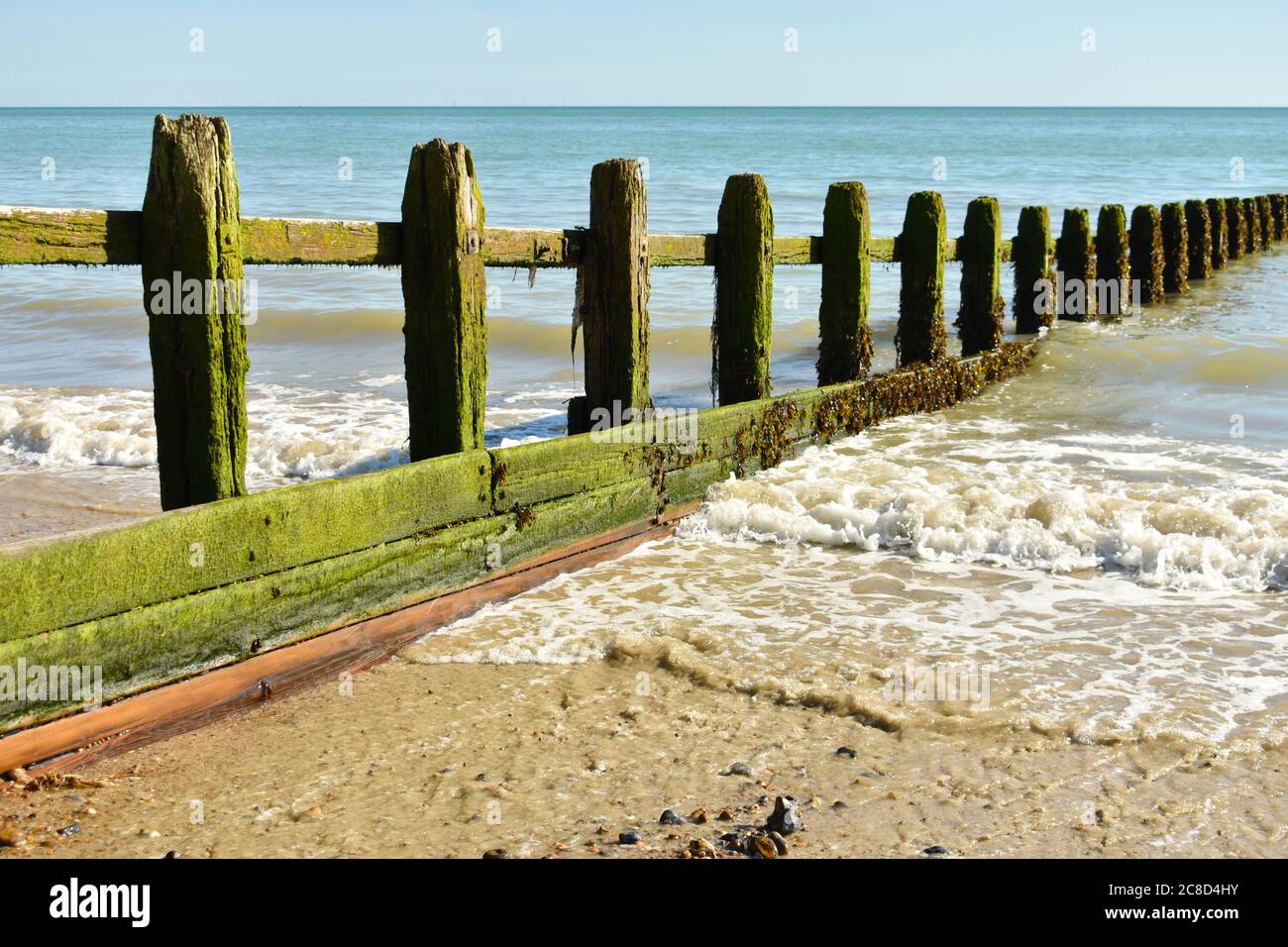 Wooden sea breaker with lapping waves on the sand and deep blue sea in ...