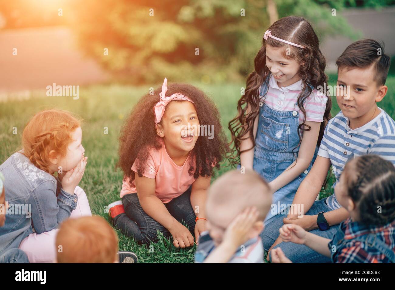 Group multi-ethnic children sitting together smiling outdoors, focus on ...