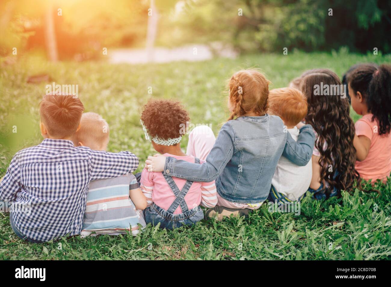 Back view of cute kids seated on green grass and relaxing. Outdoors ...