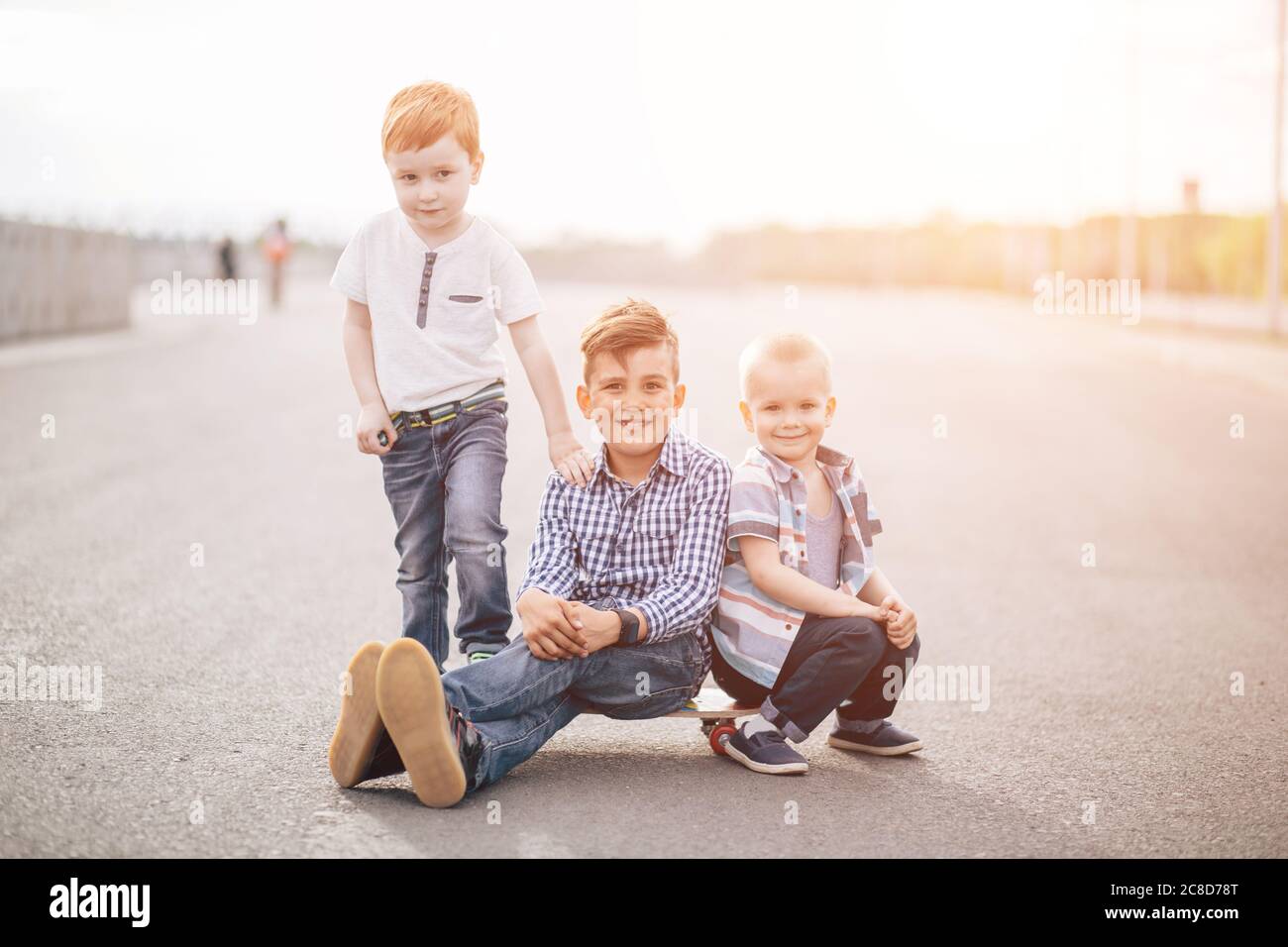 Three boys outdoor. Two boys sitting on a skateboard, one readhead boy ...