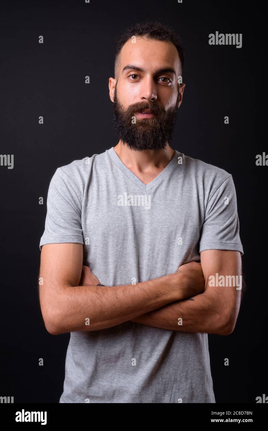 Young handsome Persian man with dreadlocks against black background ...