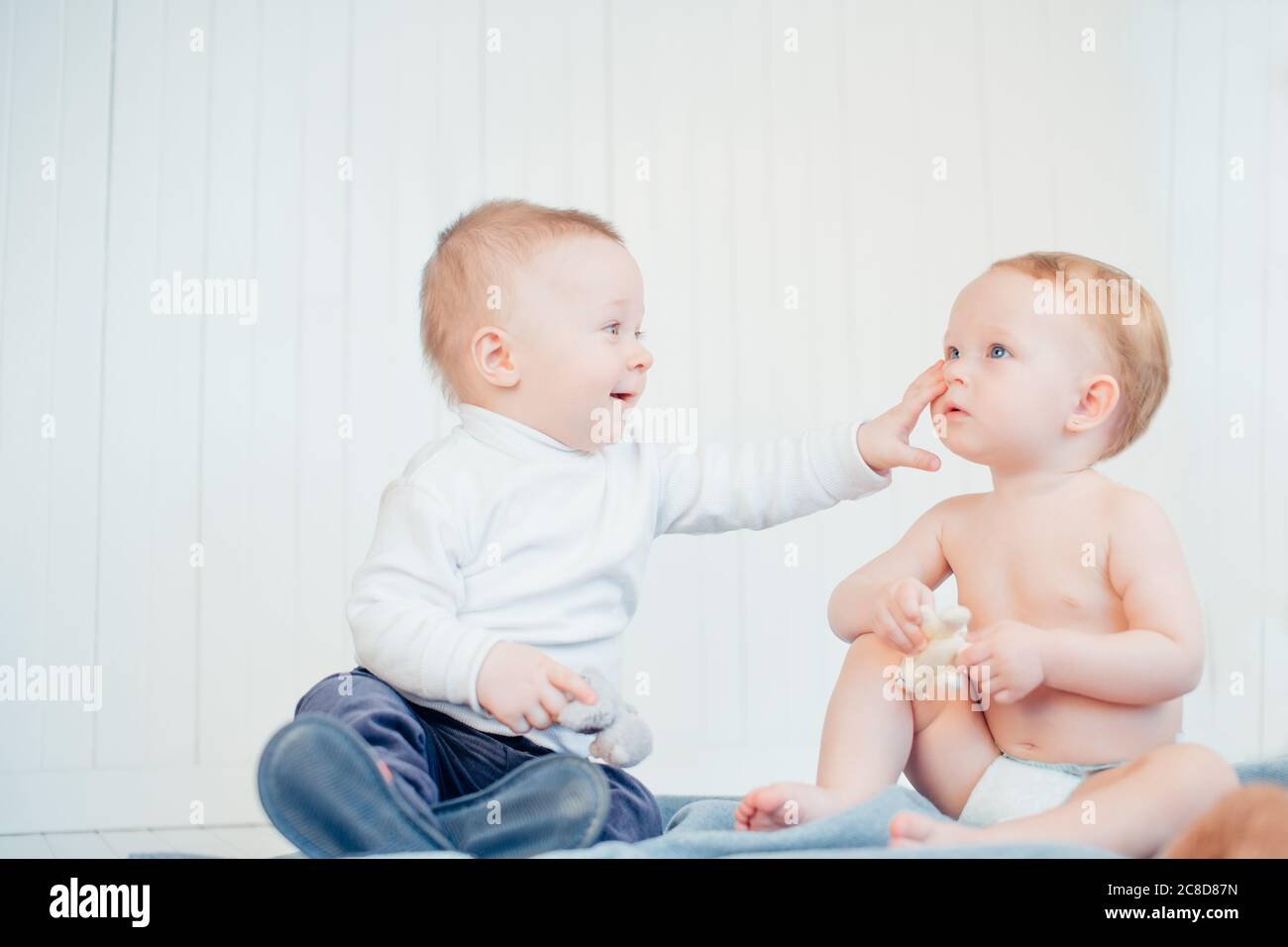 Side view of two babies playing on bed Stock Photo - Alamy