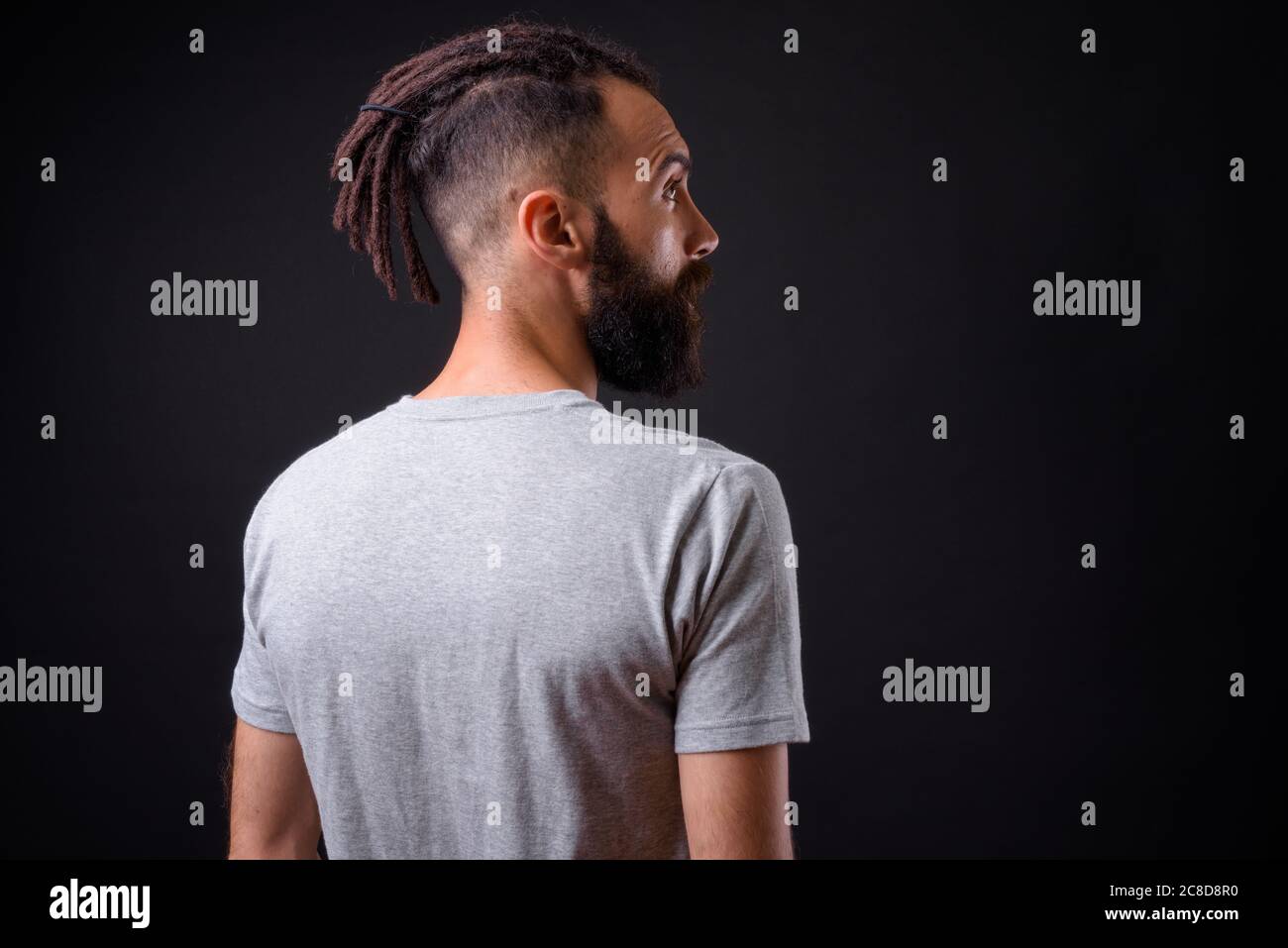 Young handsome Persian man with dreadlocks against black background ...