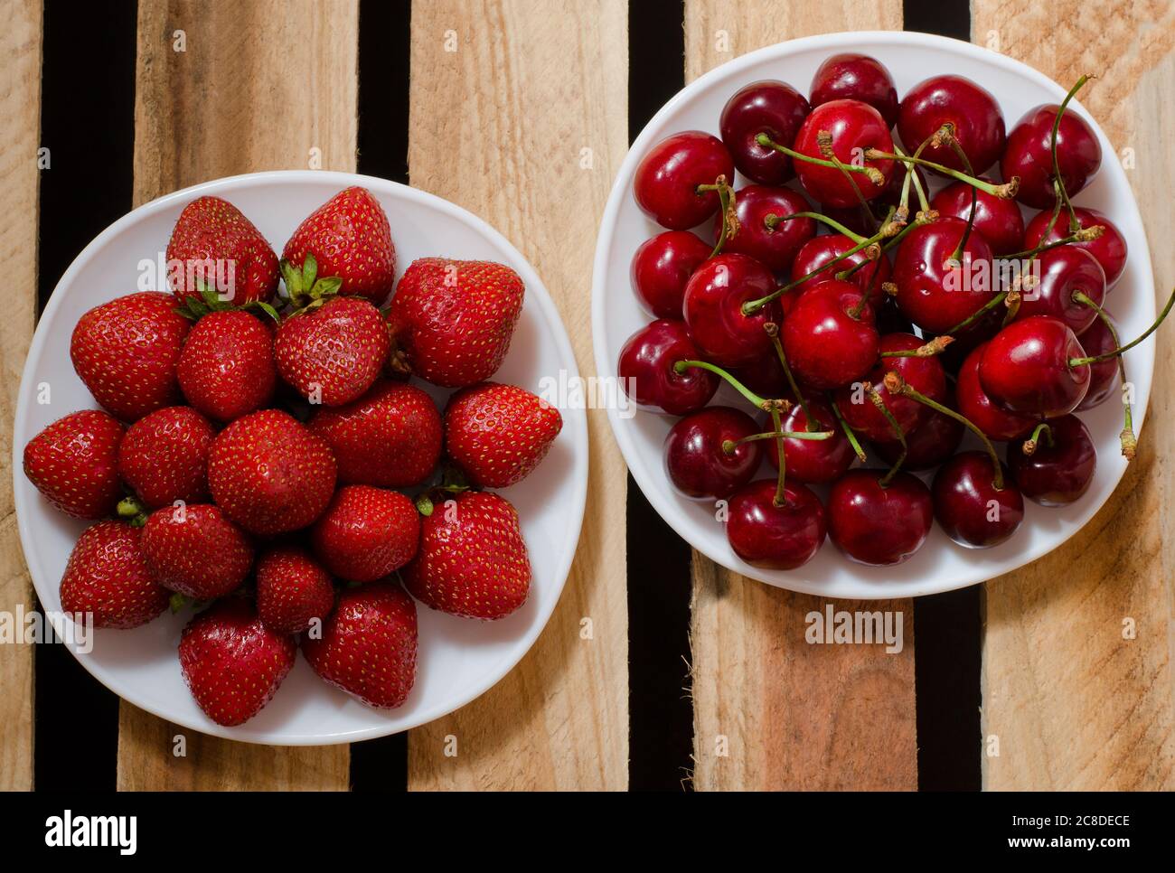 Two dishes with strawberries and cherries on wooden plates, top view ...