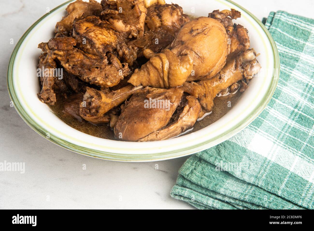 A serving of Filipino-style chicken adobo dish in a bowl with a green ...