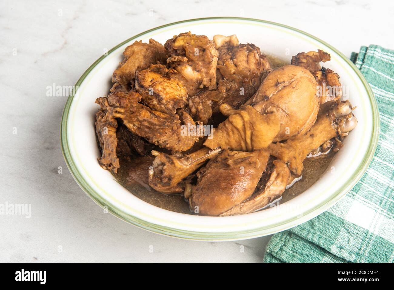 A serving of Filipino-style chicken adobo dish in a bowl with a green ...