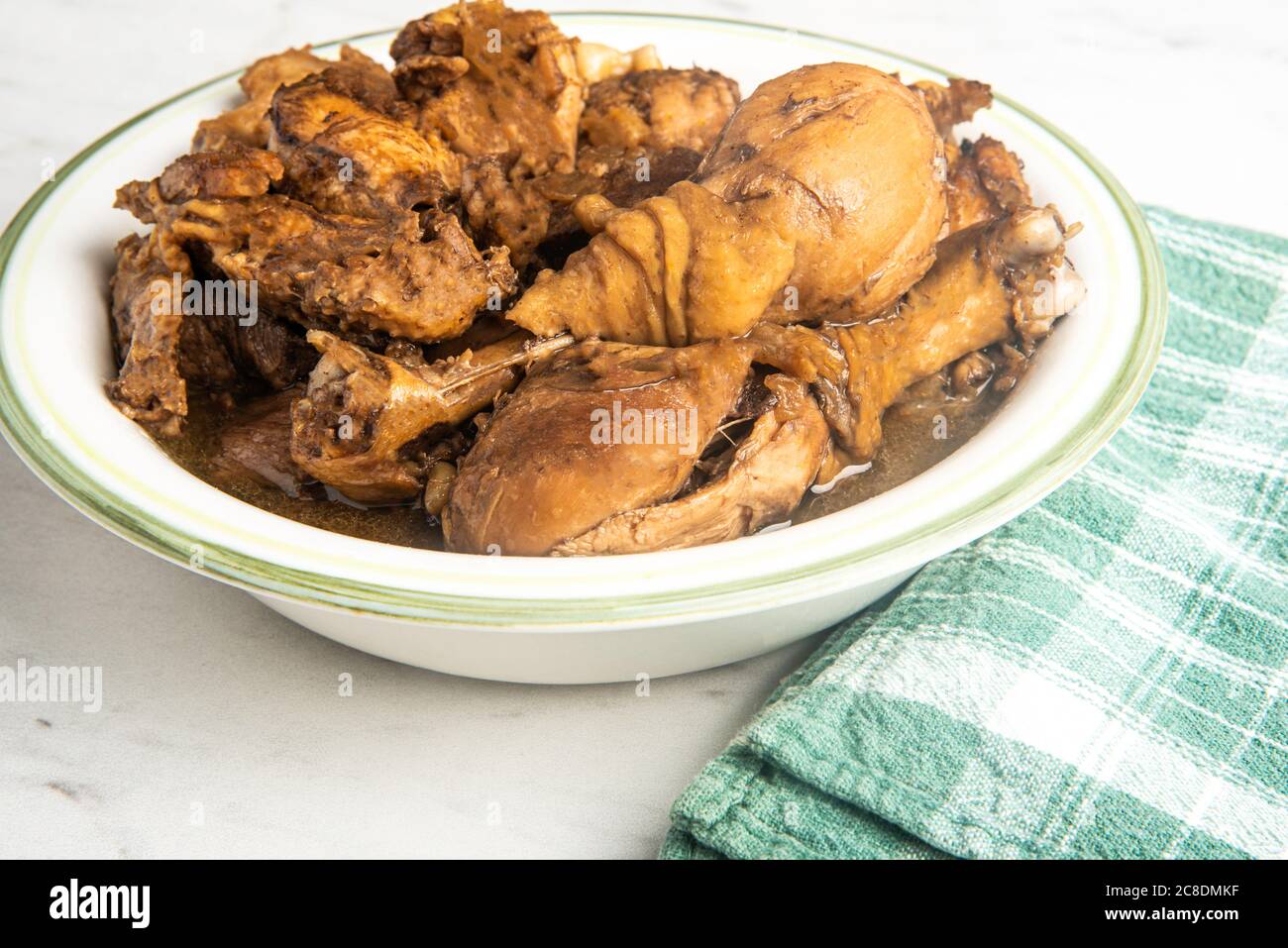 A serving of Filipino-style chicken adobo dish in a bowl with a green ...