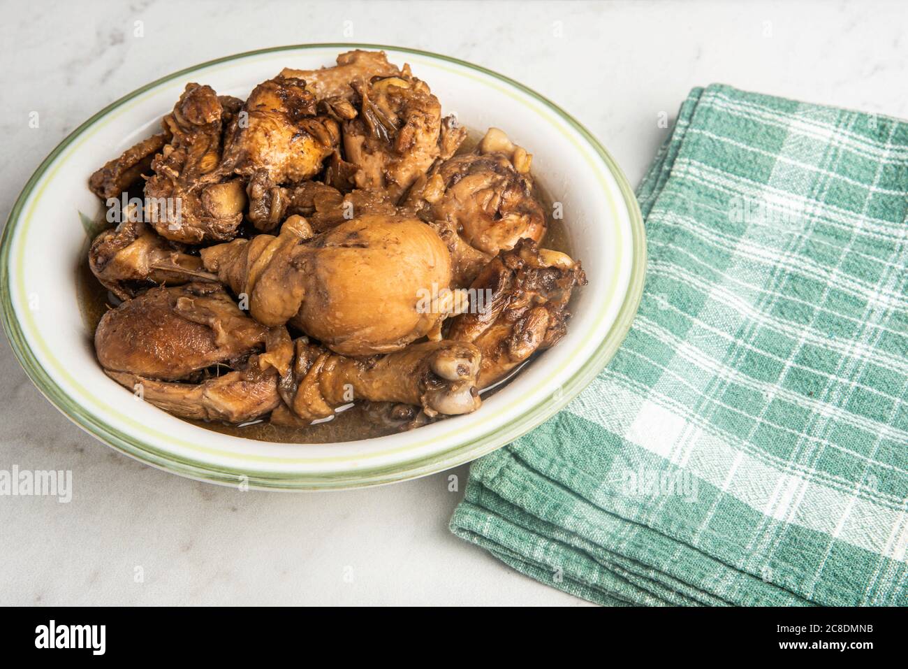 A serving of Filipino-style chicken adobo dish in a bowl with green ...