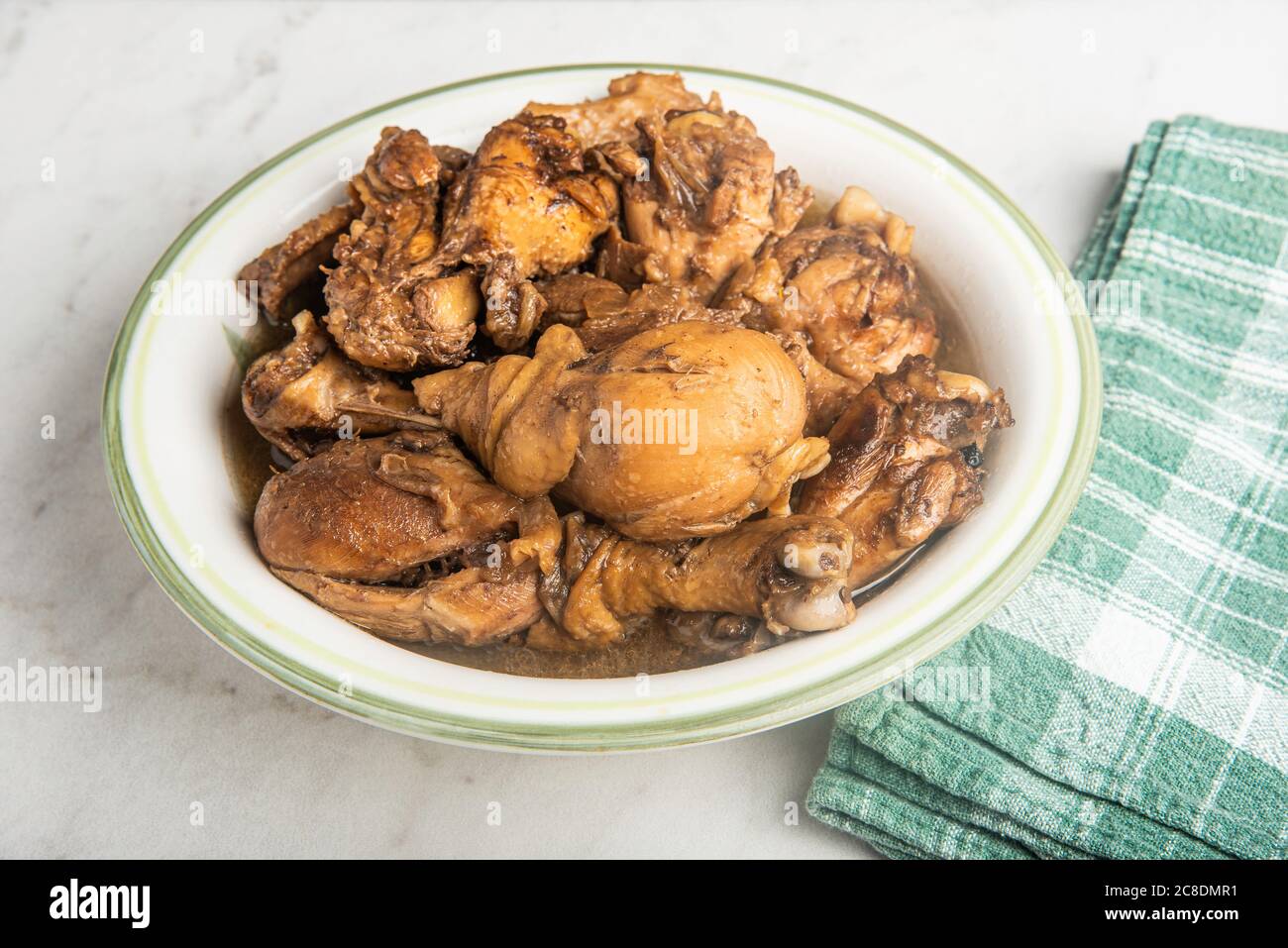 A serving of Filipino-style chicken adobo dish in a bowl with green ...