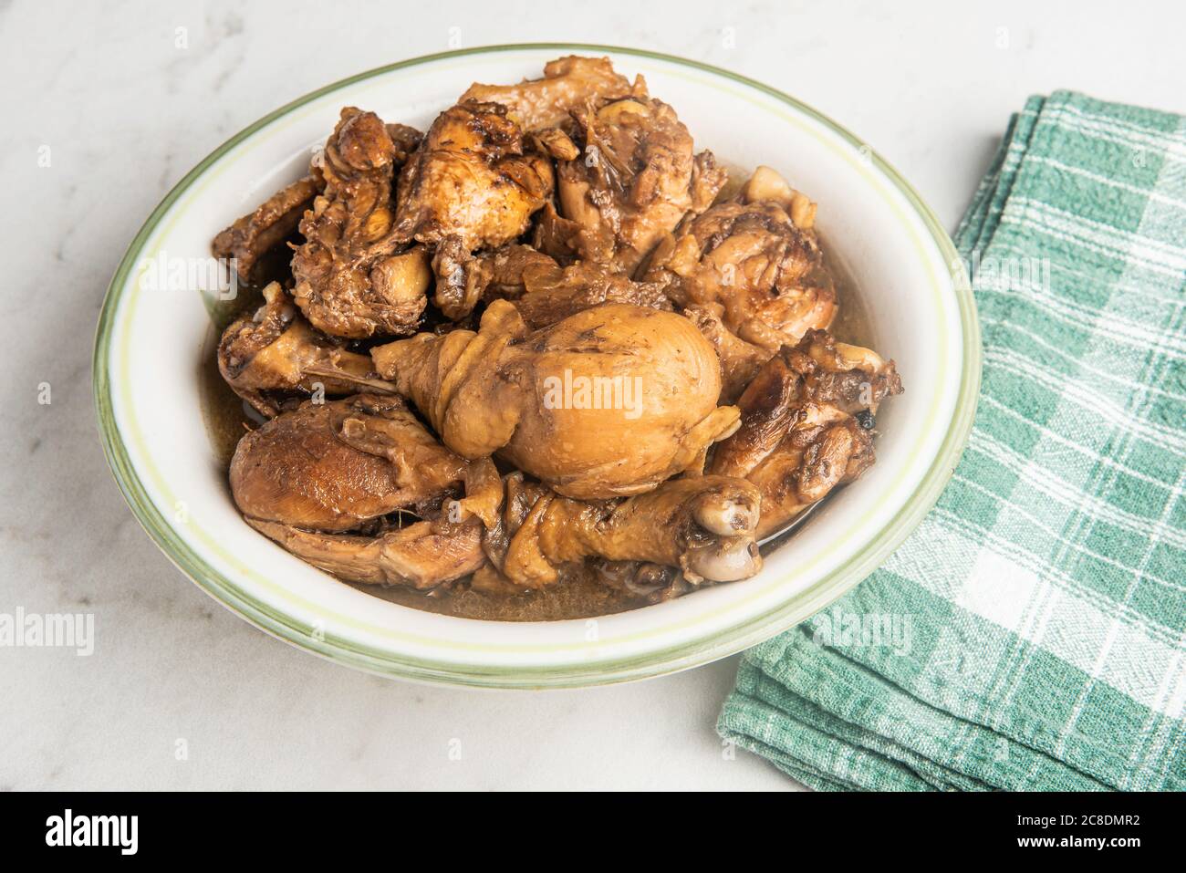 A serving of Filipino-style chicken adobo dish in a bowl with green ...