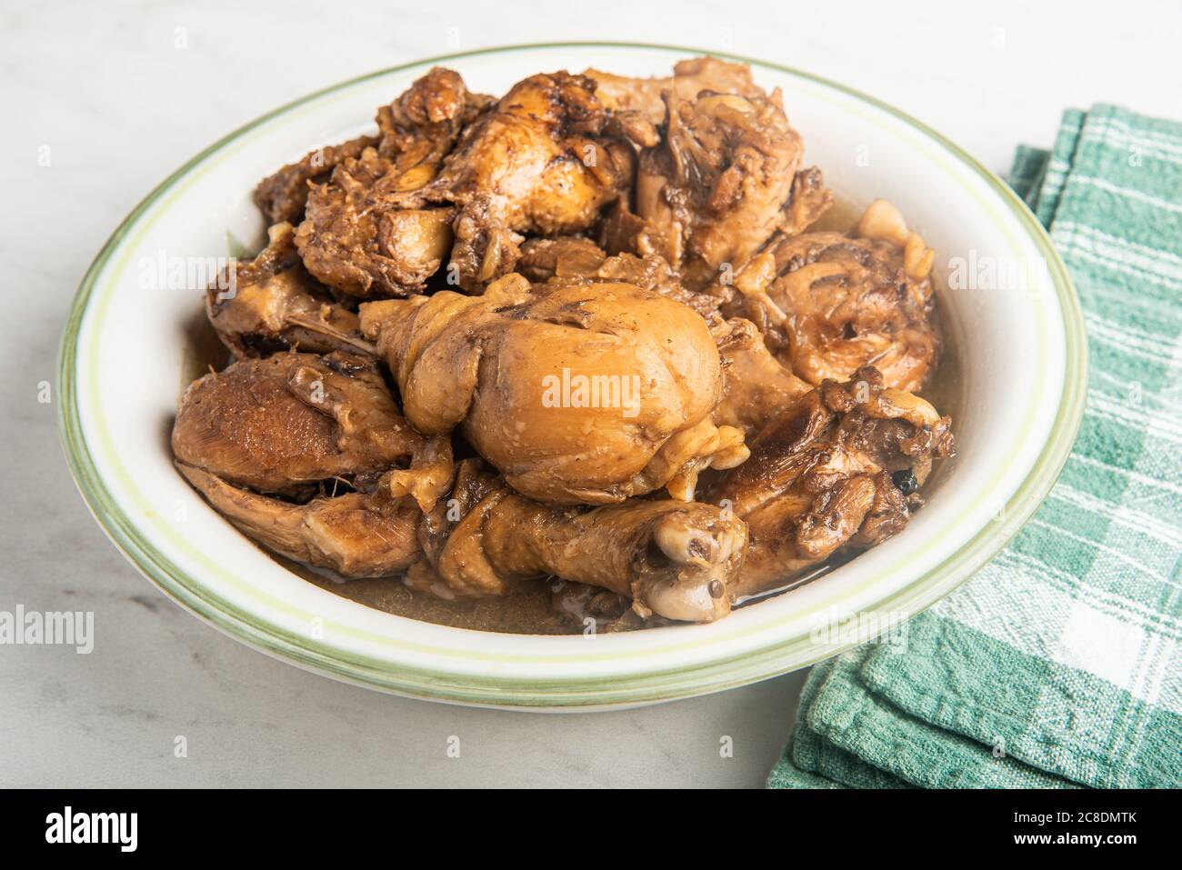 A serving of Filipino-style chicken adobo dish in a bowl with green ...