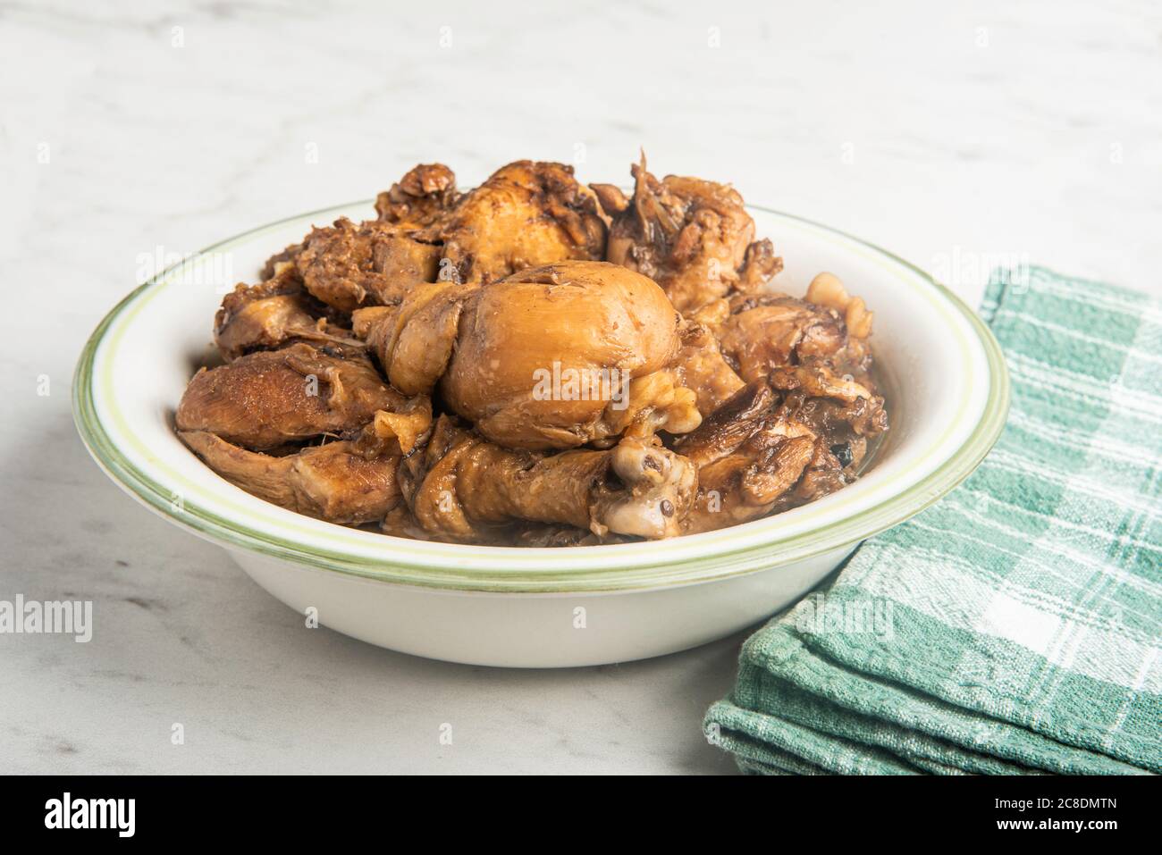 A serving of Filipino-style chicken adobo dish in a bowl with green ...