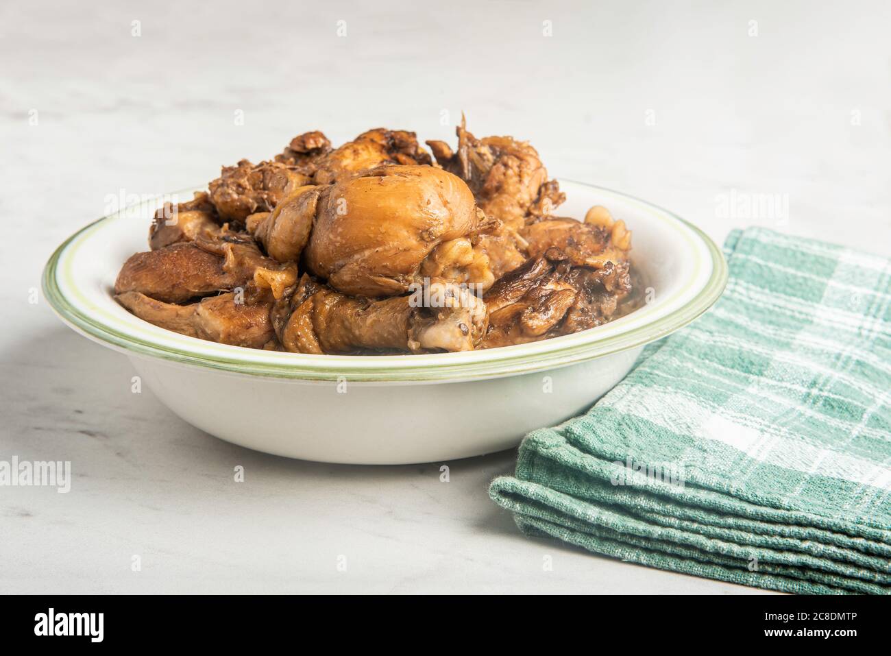A serving of Filipino-style chicken adobo dish in a bowl with green ...