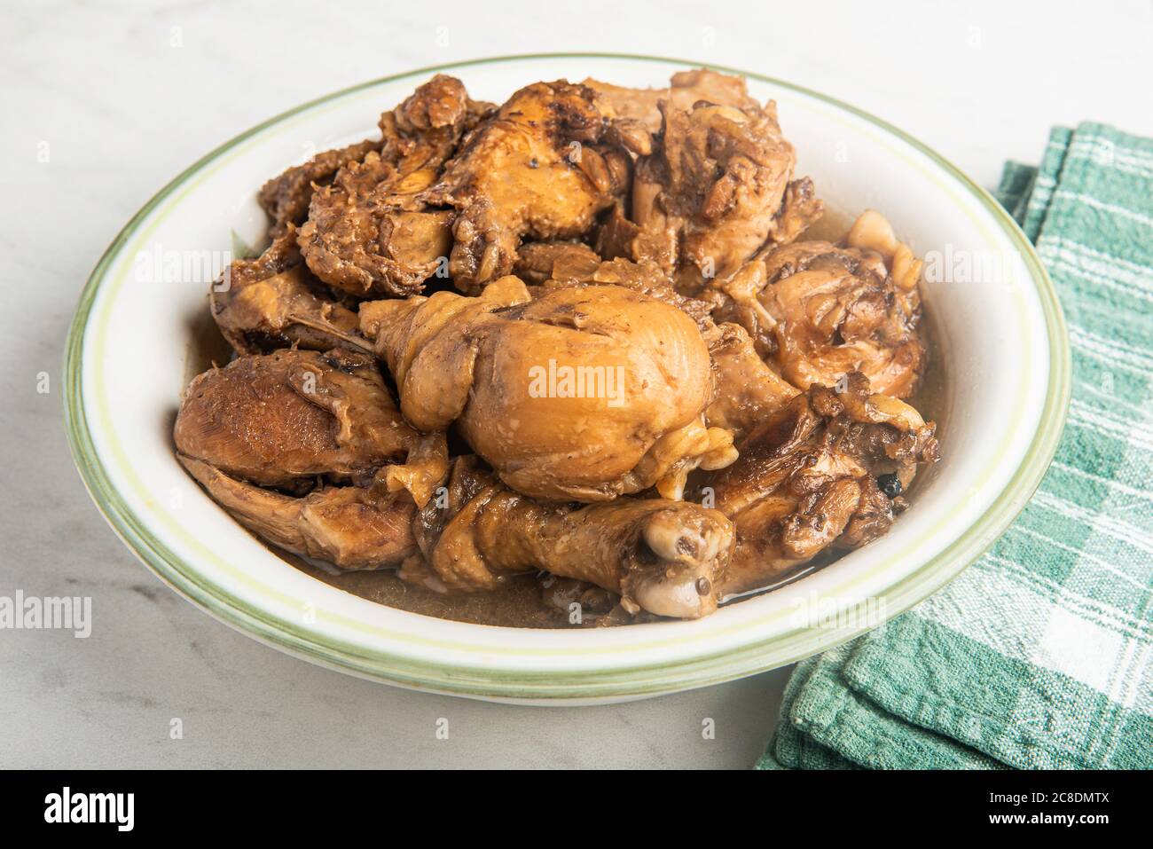 A serving of Filipino-style chicken adobo dish in a bowl with green ...
