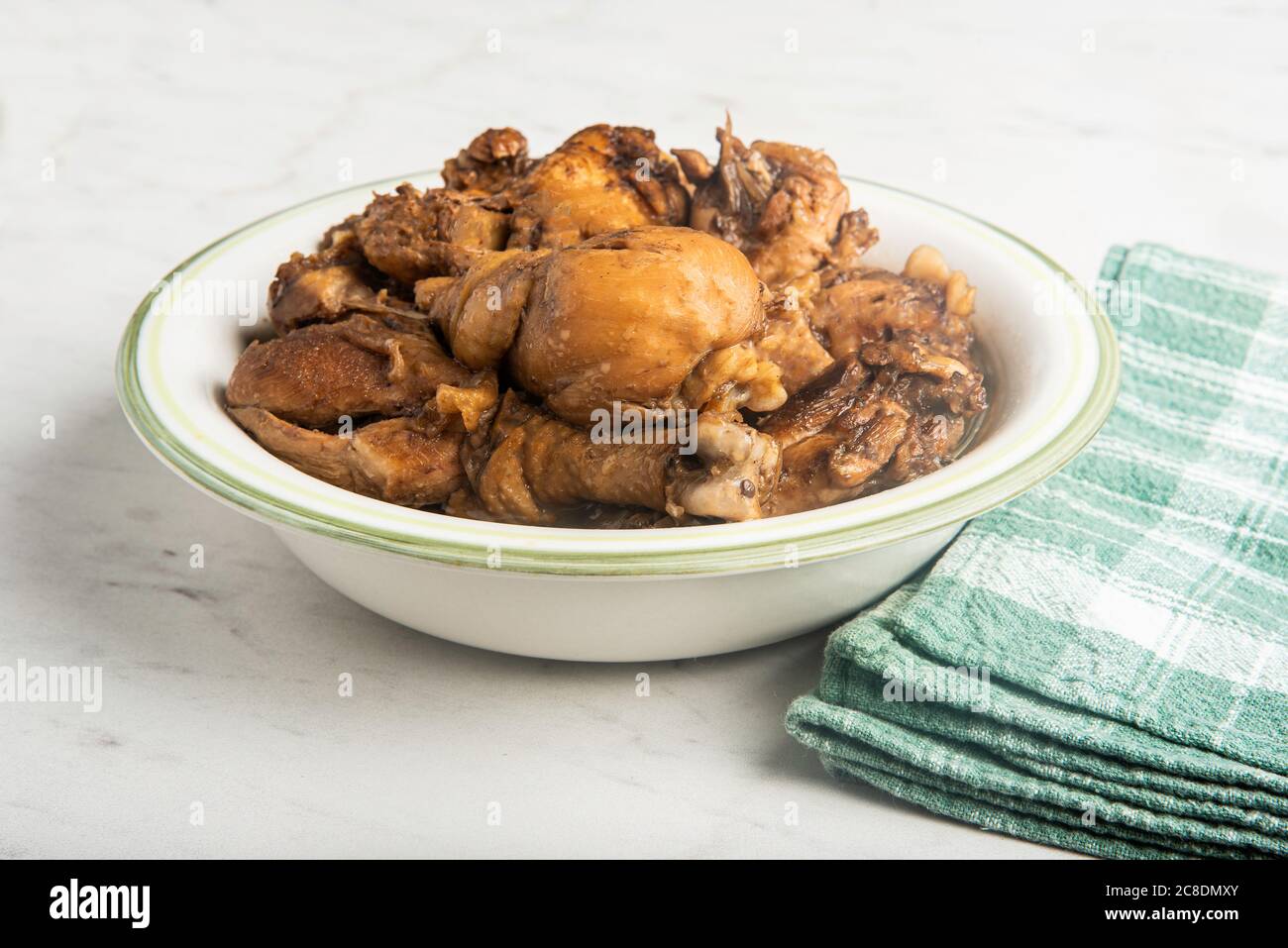 A serving of Filipino-style chicken adobo dish in a bowl with green ...