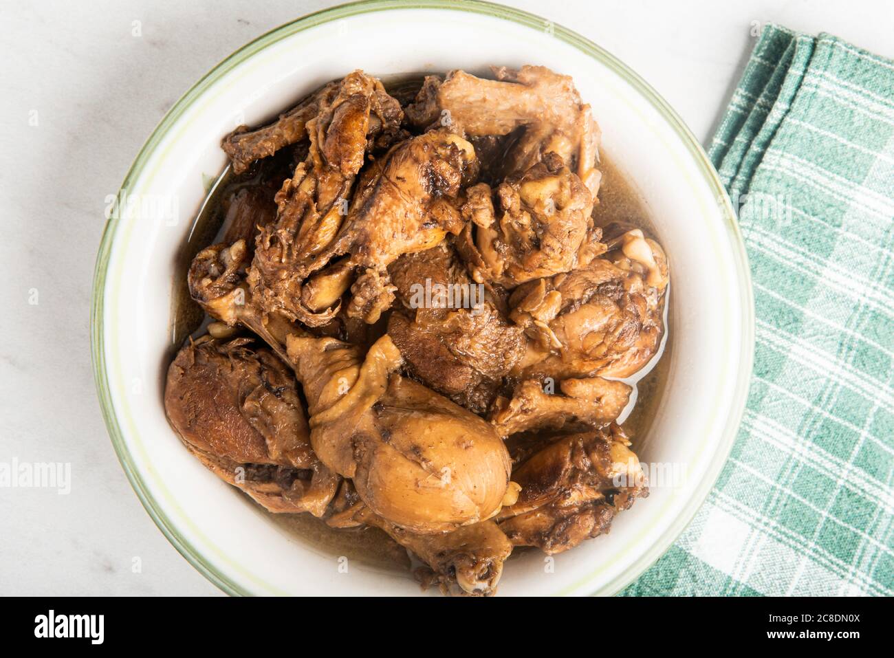 A serving of Filipino-style chicken adobo dish in a bowl with green ...