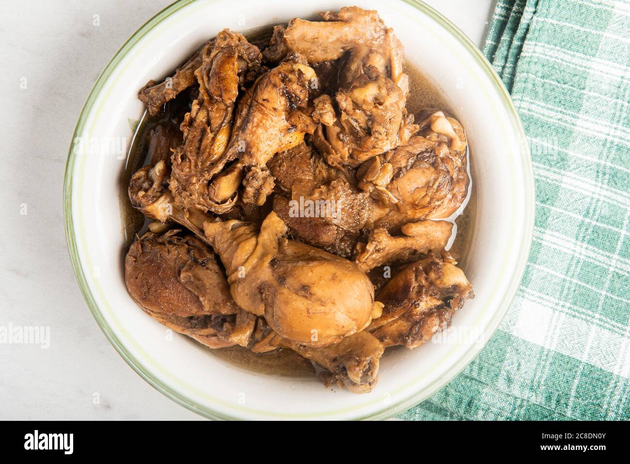 A serving of Filipino-style chicken adobo dish in a bowl with green ...